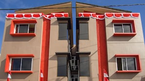 Um edifício com fachada simétrica, com dois conjuntos de janelas e uma escadaria central.