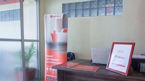 Uma mesa de recepção com um laptop, um certificado emoldurado e um banner promocional da RedDoorz.