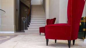 Um hall amplo com uma poltrona de veludo vermelho, uma escada e um lustre moderno.