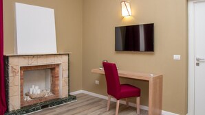 Um quarto com lareira, escrivaninha, uma cadeira vermelha e televisão montada na parede.