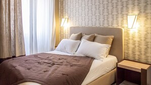 Cama bem arrumada com manta marrom e almofadas brancas, mesa de cabeceira de madeira com luminária e parede estampada.