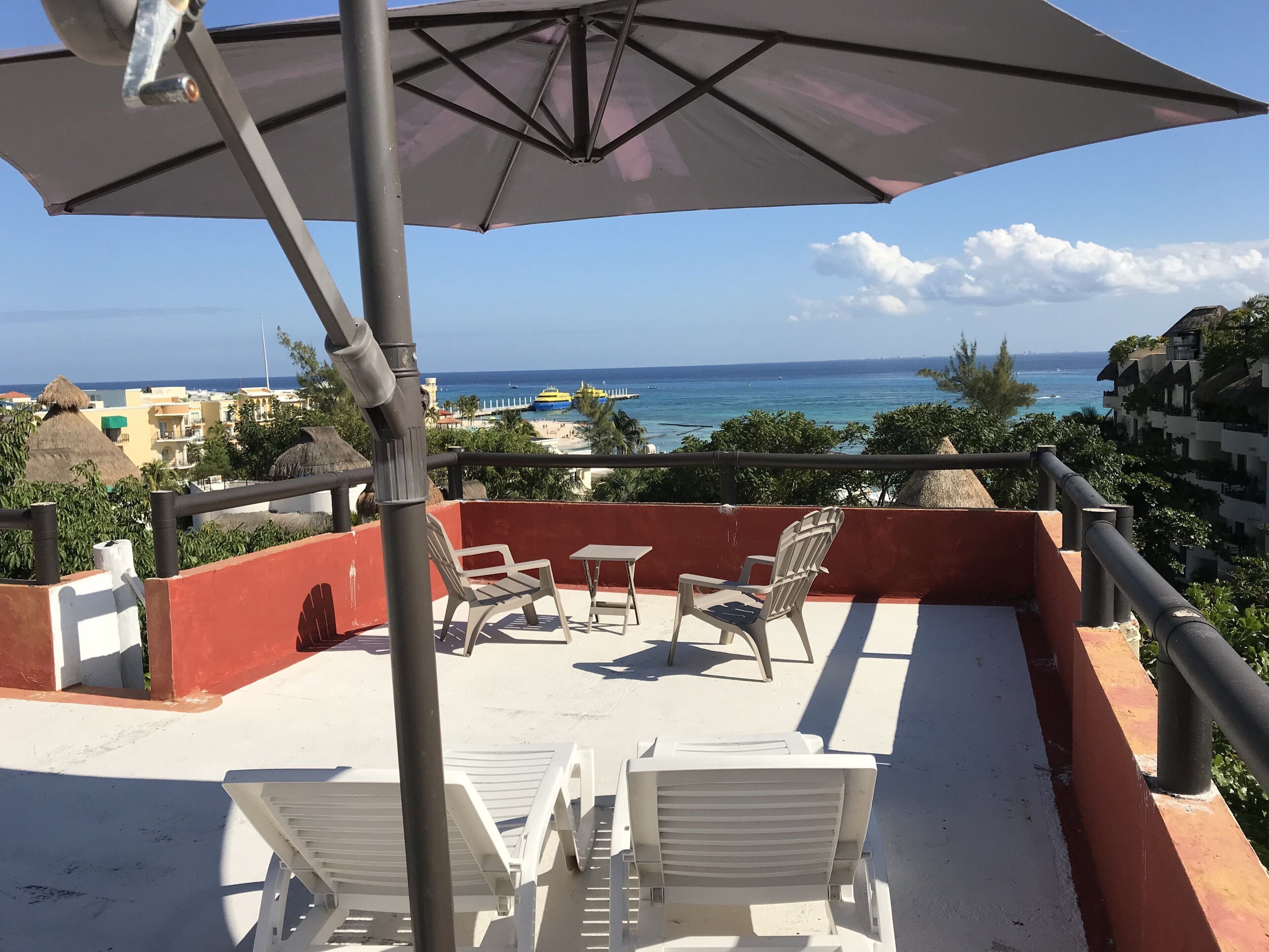 Varanda com vista para o mar, uma mesa, duas cadeiras e um guarda-sol.