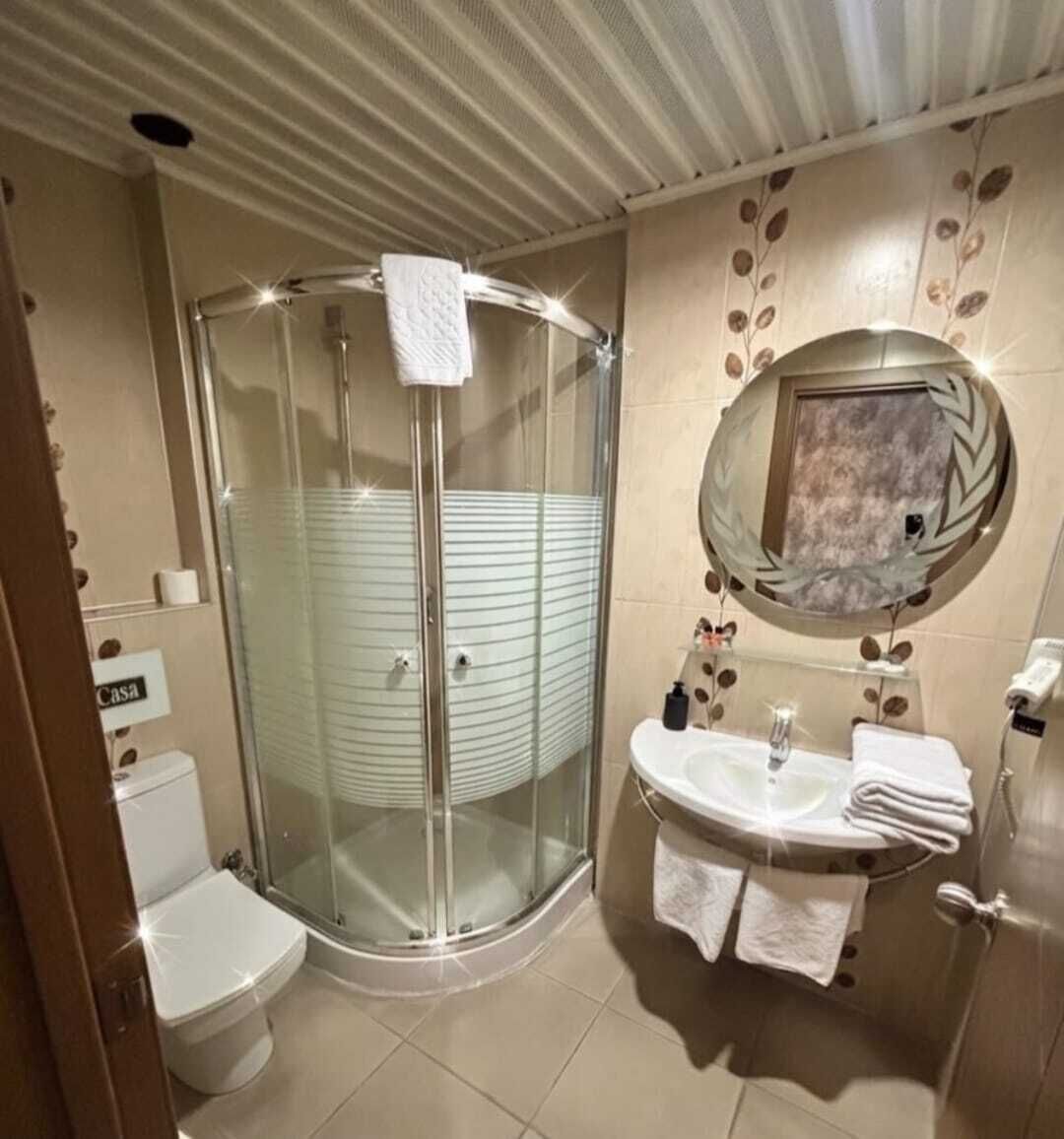 Uma casa de banho com chuveiro em cabine de vidro, sanita, lavatório com espelho e um porta-toalhas.