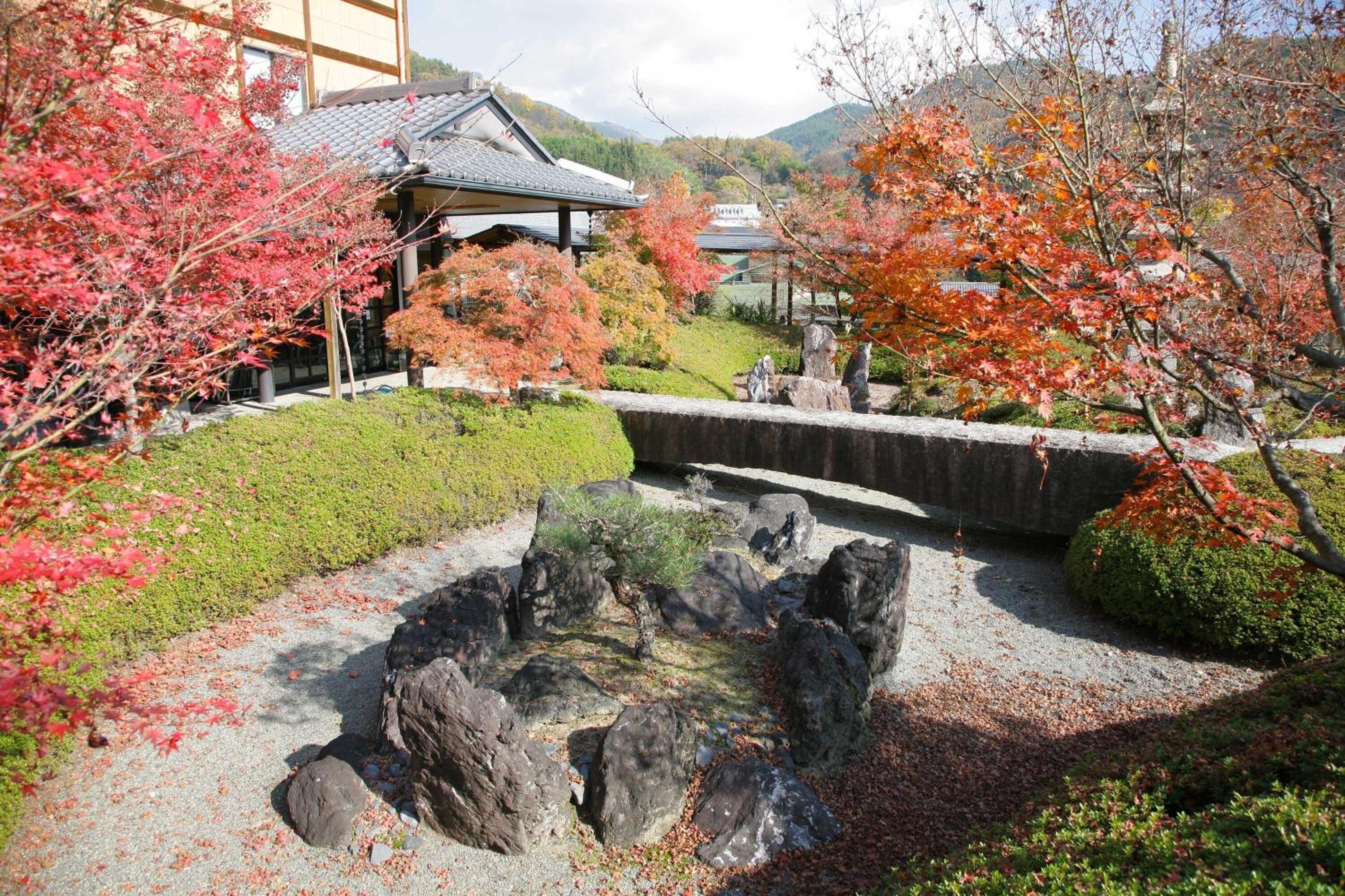 Um jardim japonês tradicional com uma ponte de pedra, um edifício com telhado de cerâmica e folhagem de outono.