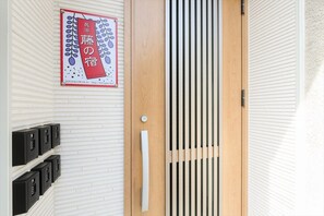 Uma área de recepção de hotel com porta de madeira, um mural com texto em japonês e vários interfones pretos na parede.