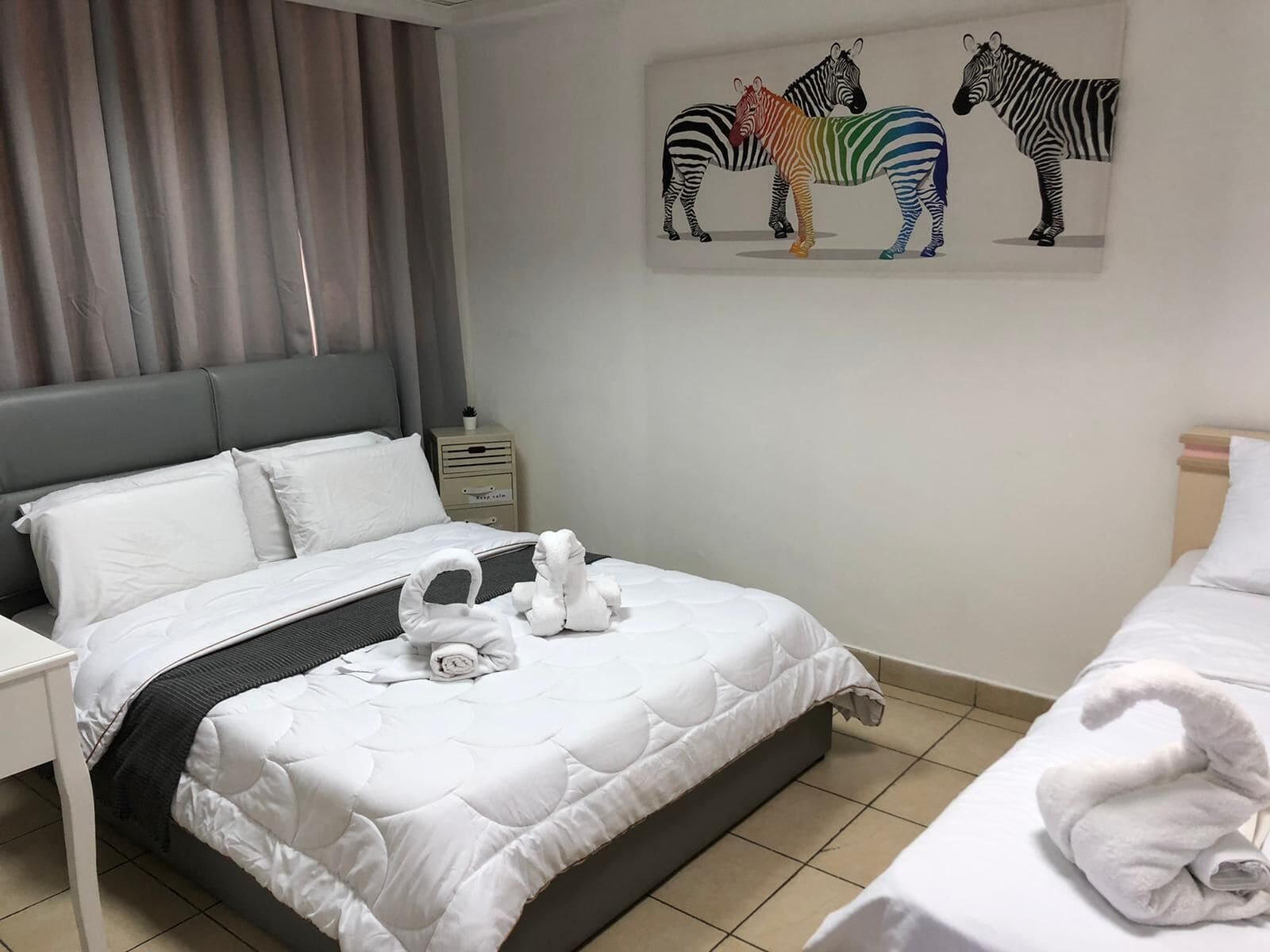 Quarto de hotel com cama, mesa de cabeceira, arte na parede com zebras e escultura de toalha.