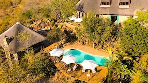 Casa com telhado de palha, piscina e área de estar, rodeada por árvores.