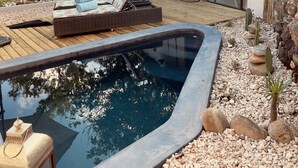 Uma área de piscina com deck de madeira, espreguiçadeiras e uma estrutura com telhado de palha.