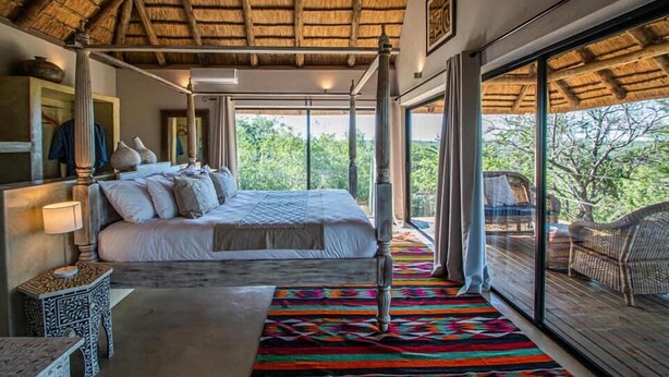 Quarto espaçoso com uma cama grande, um ventilador de teto e vista para o exterior por grandes janelas.