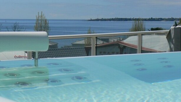 Piscina azul cristalina com hidromassagens, rodeada por uma varanda com vista para o mar.