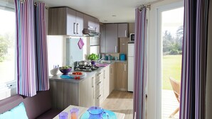 Uma cozinha moderna com uma ilha central, uma área de refeições com mesa e cadeiras, e vista para o exterior através de amplas janelas.