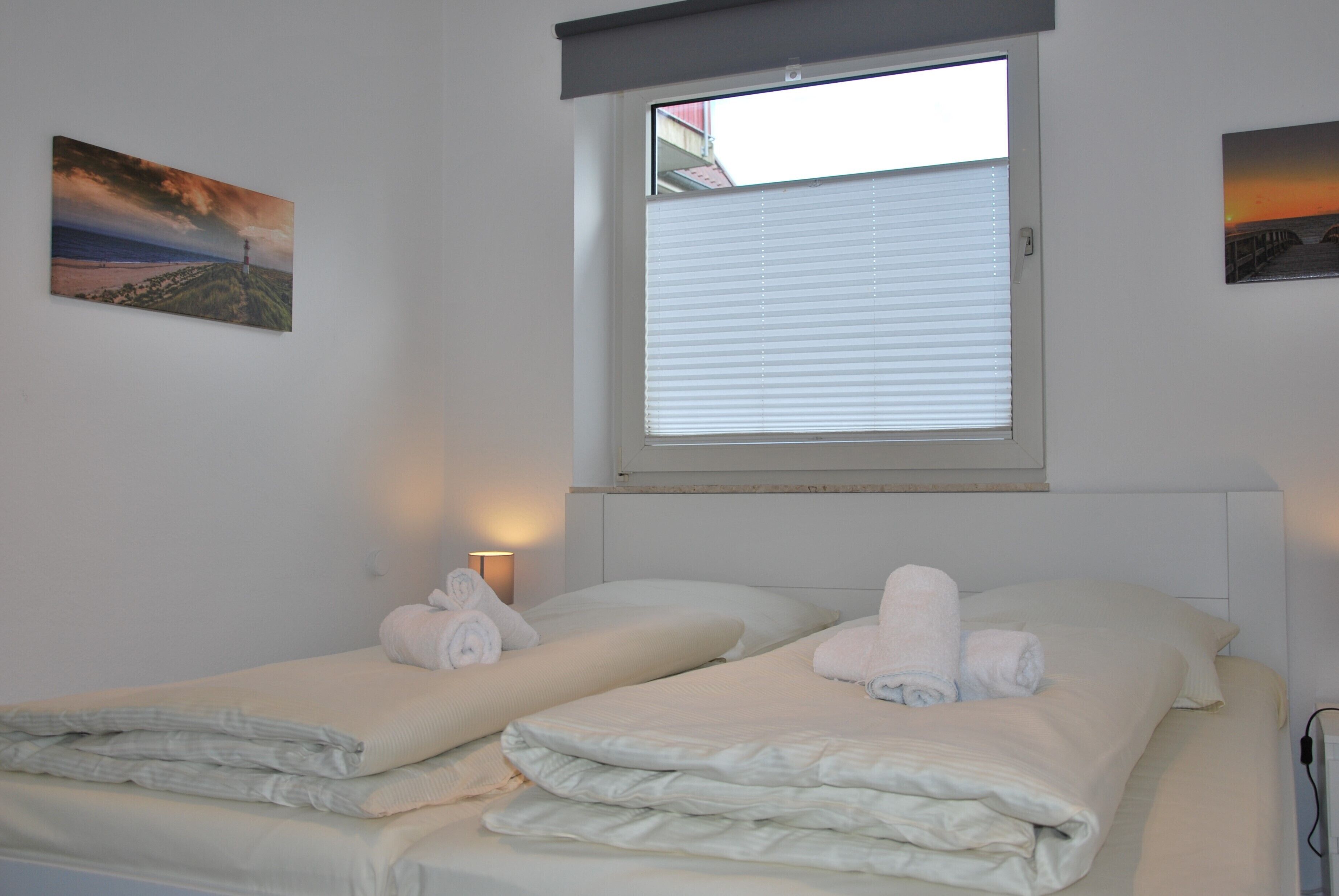 Quarto com duas camas, janela com persianas e duas luminárias fixadas na parede.