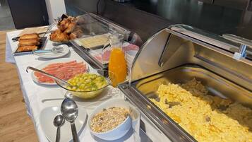 Buffet com ovos mexidos, fiambre, croissants e uma saladeira de frutas.