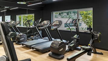 Academia com várias esteiras, bicicletas ergométricas e piso de madeira.