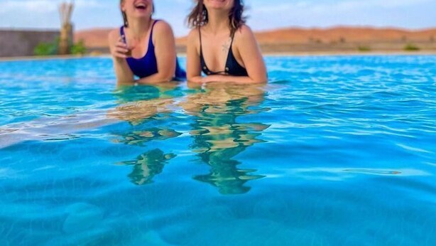 Duas pessoas em uma piscina azul cristalina, com paisagem desértica ao fundo.
