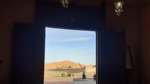 Porta aberta que dá para um pátio com tapete estampado, duas lanternas penduradas e vista para uma paisagem desértica.