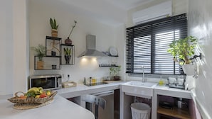 Uma cozinha moderna com máquina de lavar louça embutida, micro-ondas e pia. Há plantas em vasos nas prateleiras e uma cesta de frutas no balcão.