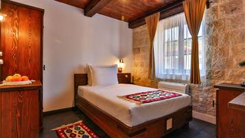 Uma cama de madeira num quarto com paredes de pedra, uma mesinha de cabeceira e uma cesta de frutas.