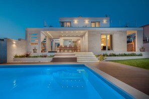 Uma casa moderna de dois andares, com piscina, área de estar externa e entrada bem iluminada.