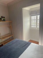 Um quarto com uma cama, uma prateleira de madeira e uma janela.