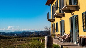 Um edifício amarelo com varandas, mesas ao ar livre e vista para montanhas.
