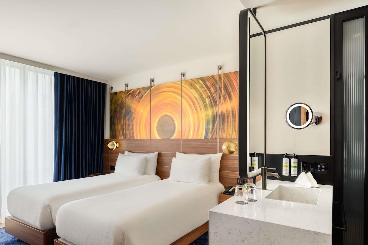 Quarto de hotel com uma cama grande, banheiro com espelho e vista da cidade.