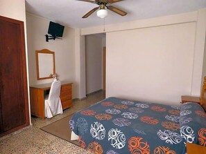 Quarto com cama, penteadeira, espelho, ventilador de teto e televisão na parede.