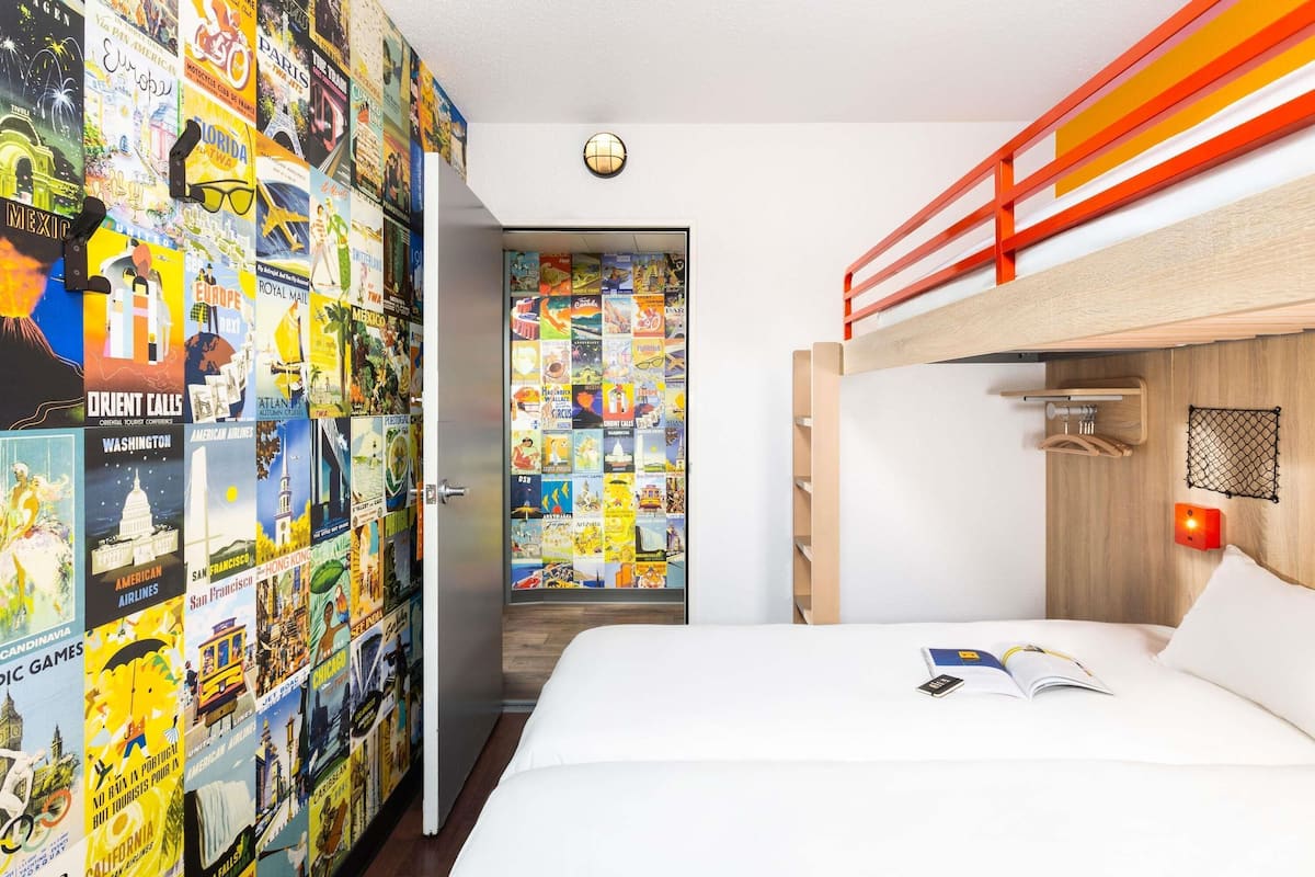 Um quarto com uma cama beliche, uma parede decorada com cartazes de viagens, uma porta e uma pequena janela.