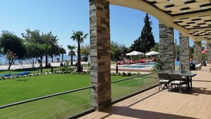 Uma área externa coberta com piscina, espreguiçadeiras e vista para a praia.