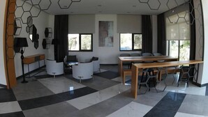Interior moderno com piso xadrez, área de jantar com cadeiras hexagonais e um espaço de estar com sofás e uma mesa de centro.