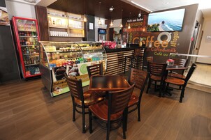 Um café com balcão de exposição de doces e bebidas, cadeiras de madeira e balcão com máquina de café.