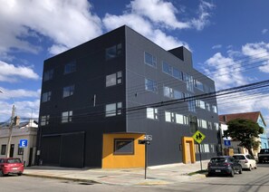 Um edifício moderno, de vários andares, com telhado plano, janelas amplas e entrada amarela.