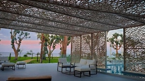 Uma área de estar coberta ao ar livre com vista para a piscina, apresentando um teto treliçado e mobiliário para exterior.