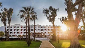 Um hotel com um pátio central, palmeiras e uma montanha ao fundo.