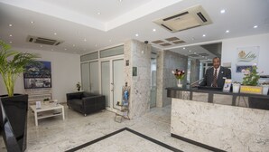 Área de recepção de hotel com piso de mármore, balcão de atendimento, um sofá e uma mesa de centro.