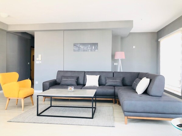 Uma sala de estar moderna com um sofá seccional cinza, uma poltrona amarela e uma mesa de centro.
