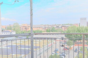 Vista de uma varanda com grade de metal, com vista para um estacionamento com vários carros e um campo esportivo.