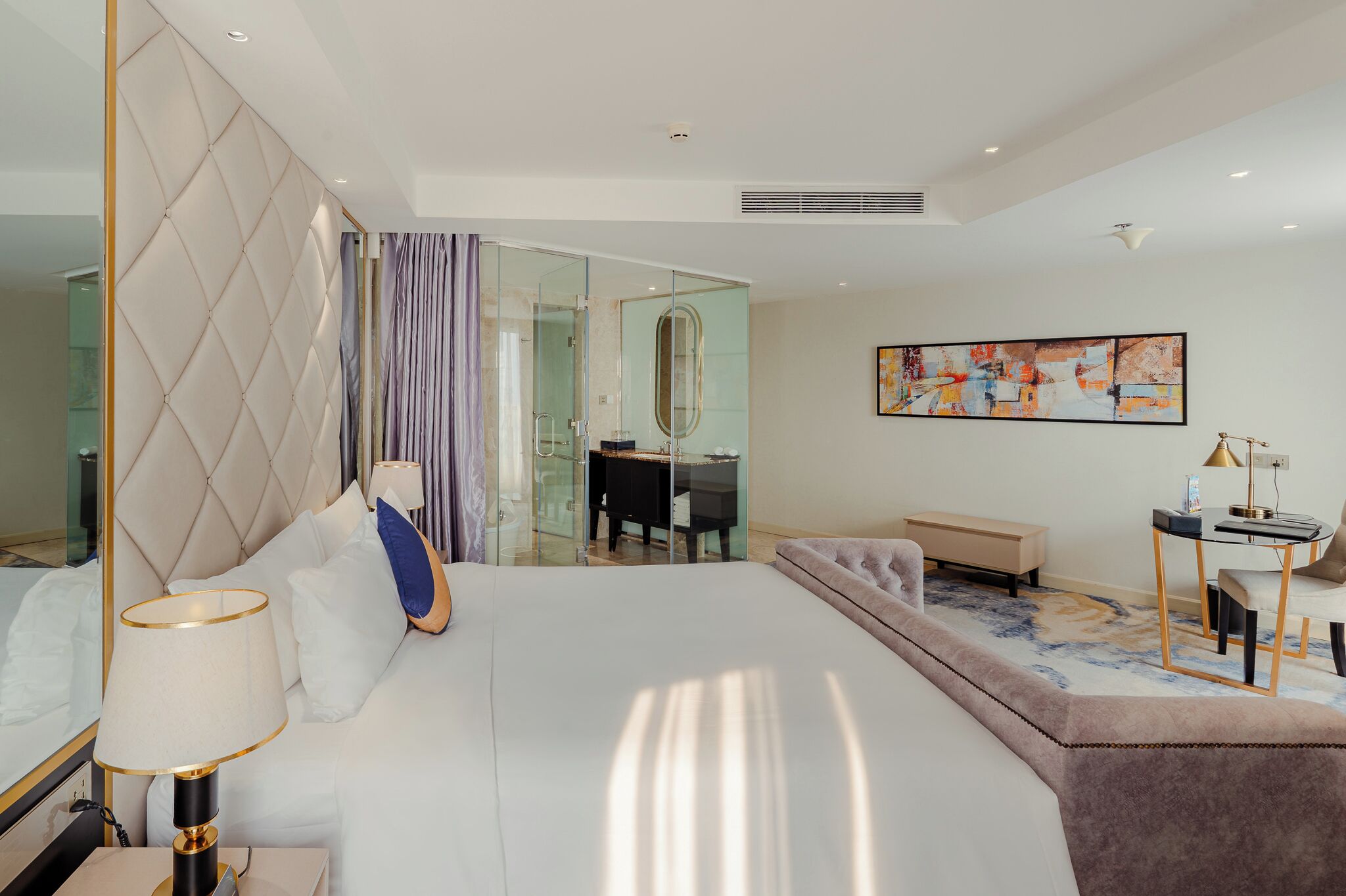 Quarto de hotel moderno com uma cama grande, uma escrivaninha, uma cadeira, um abajur e um quadro na parede.