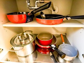 Uma cozinha com panelas e frigideiras de aço inoxidável nas prateleiras, uma frigideira vermelha e uma frigideira preta no balcão.
