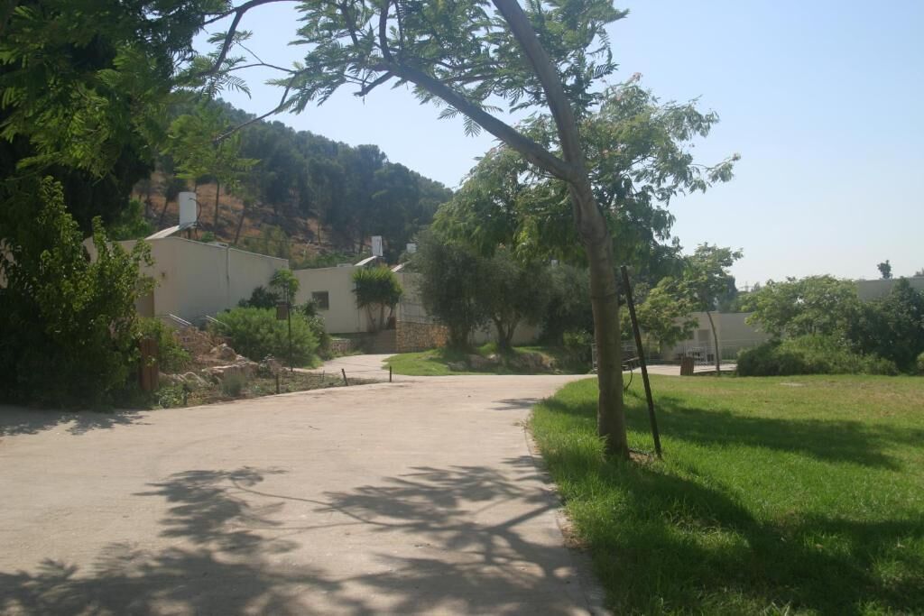 Uma trilha pavimentada que conduz a um edifício com muro de pedra e área gramada com árvores.