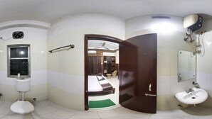 Casa de banho com sanita, bidé, lavatório, espelho e porta que dá para um quarto com cama e uma pequena mesa.