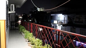 Varanda com corrimão de metal vermelho, plantas em vasos e vista de prédios à noite.