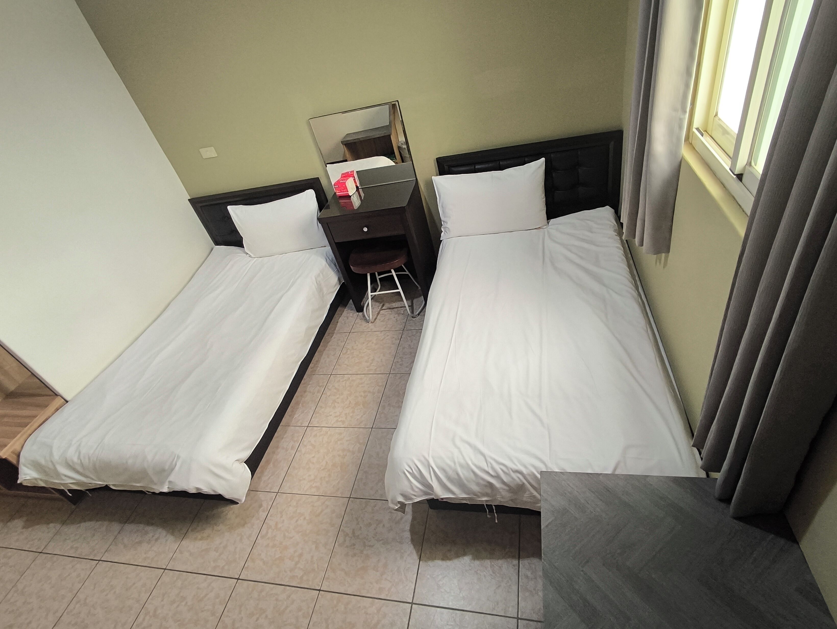 Quarto com duas camas de solteiro, uma pequena escrivaninha e uma cadeira.