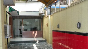 Um corredor estreito com piso de azulejos, um balcão de recepção e uma porta de vidro que dá para o interior.