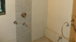 Casa de banho com parede de mármore, chuveiro, sanita e lavatório com espelho.