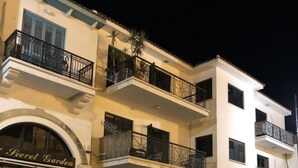 Um edifício de vários andares com varandas, um café chamado "Secret Garden" e um aviso de estacionamento.