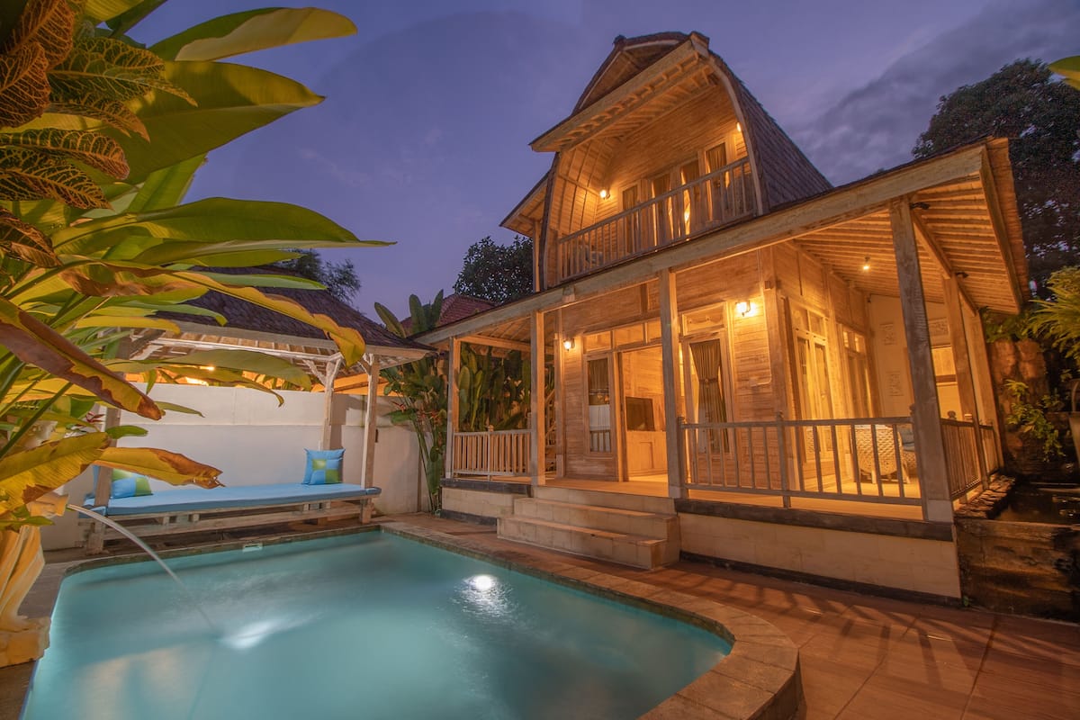 Uma casa de dois andares com piscina, varanda coberta e jardim com plantas tropicais.