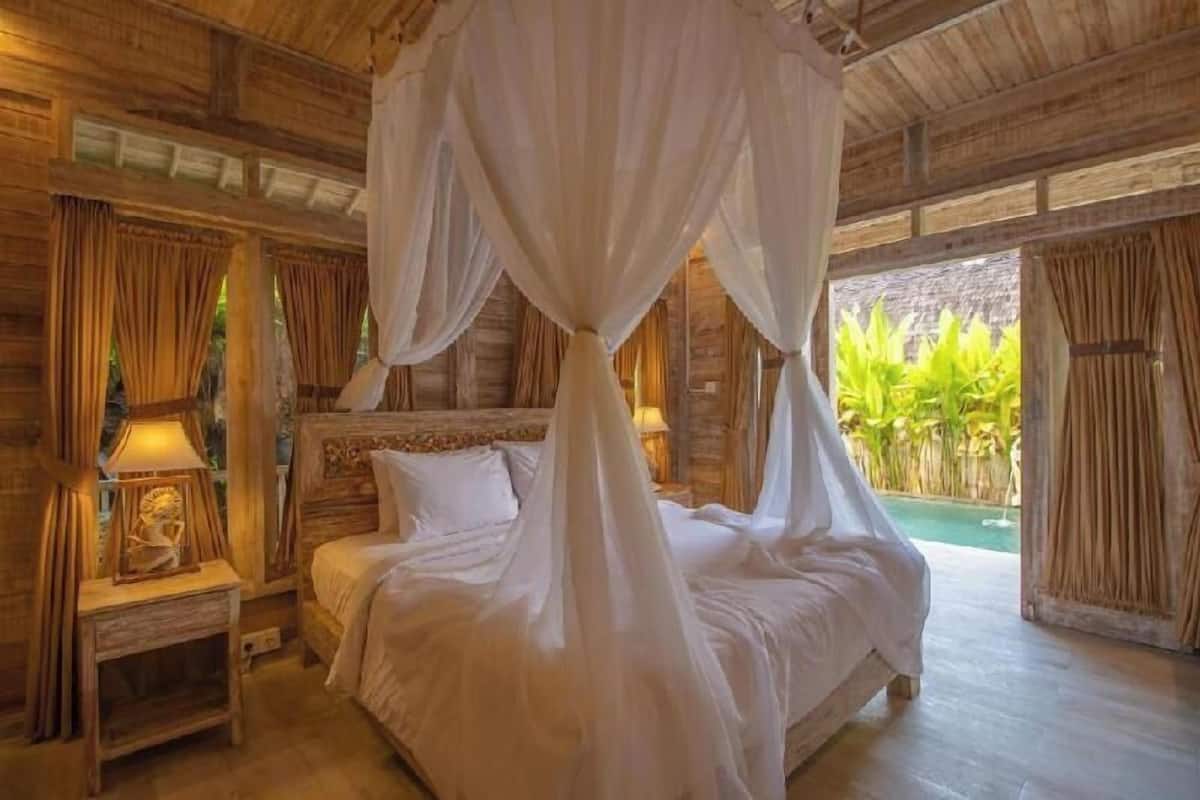 Quarto de madeira com cama, cortinas, mesa de cabeceira e abajur.