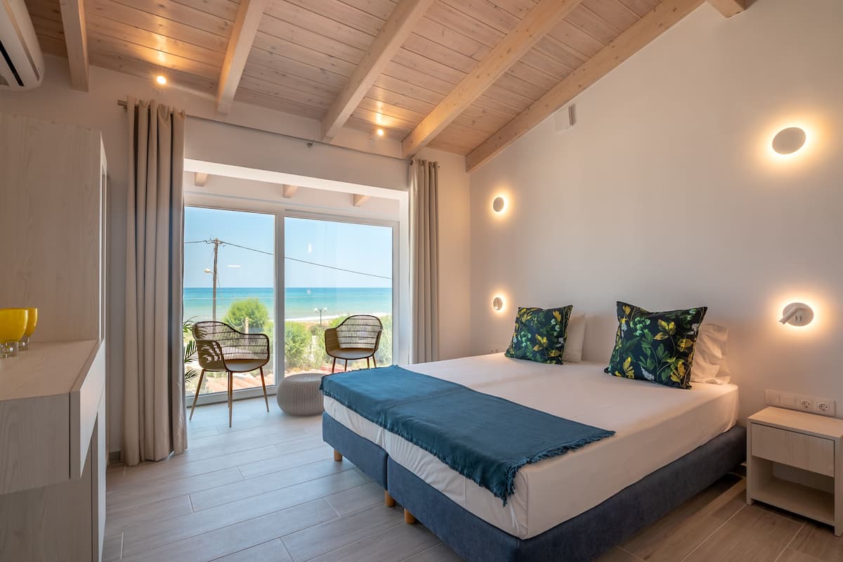 Quarto com cama grande, escrivaninha, cadeira e vista para a praia.