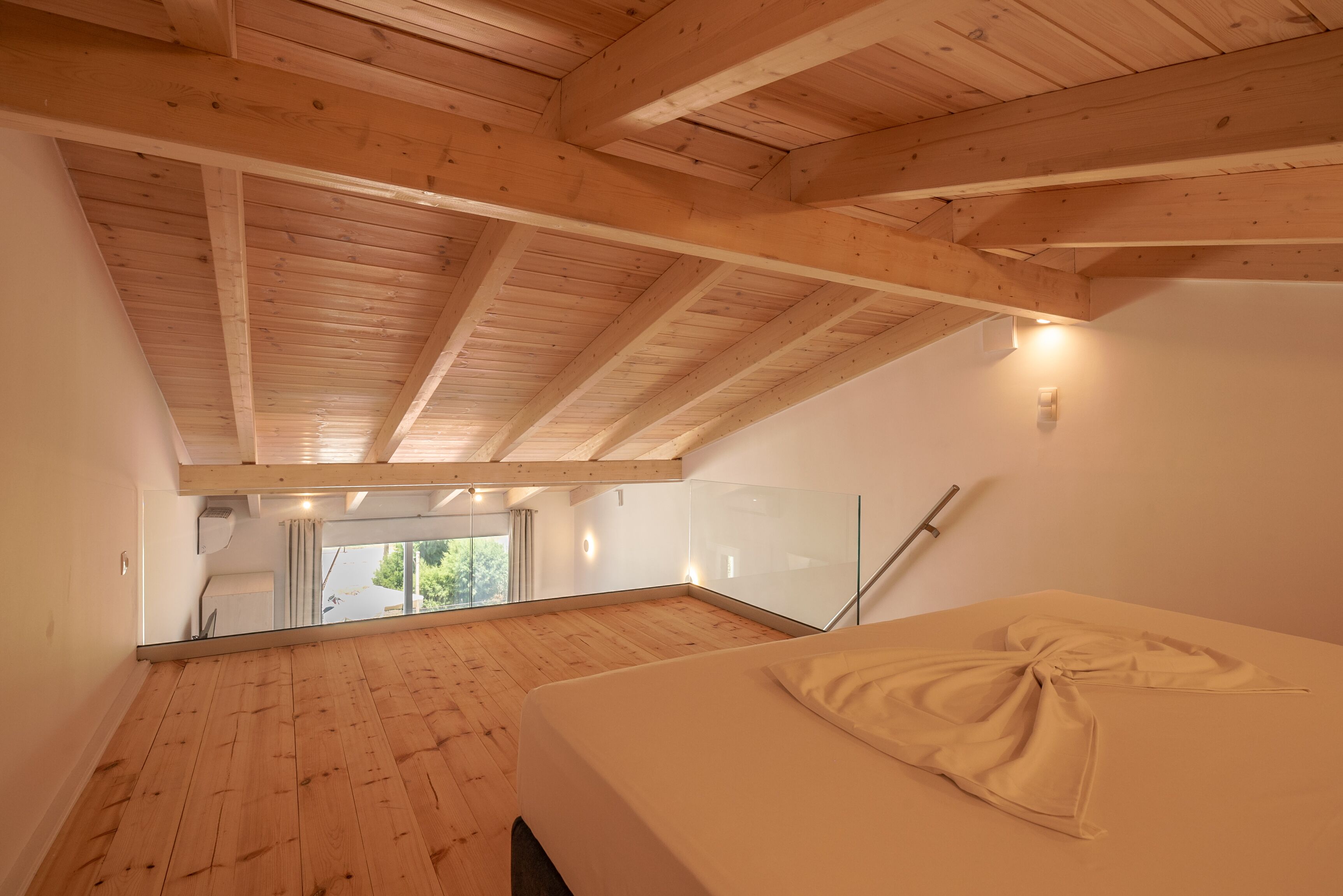 Quarto com vigas de madeira, uma cama, uma janela e vista para o exterior.